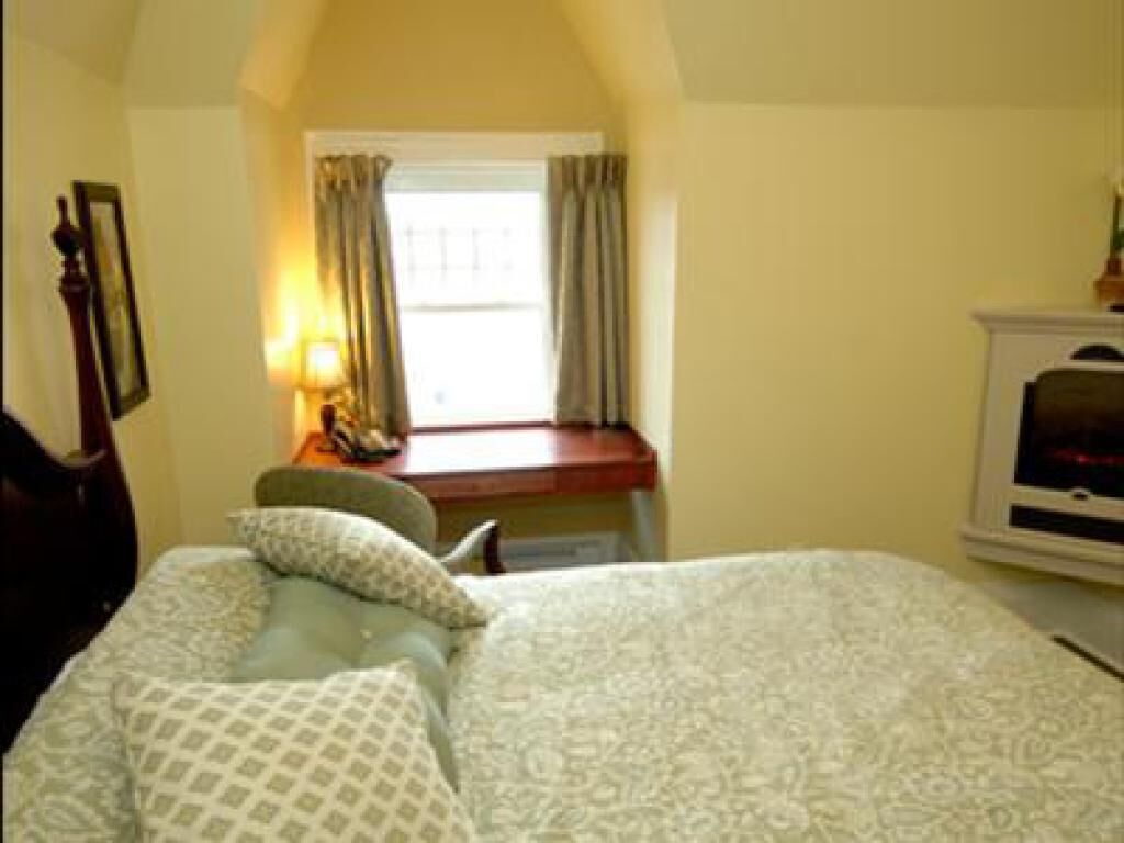 Quarto com cama, escrivaninha e janela com cortinas.