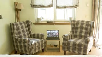 Quarto com duas poltronas xadrez, uma pequena mesa com um laptop, uma luminária e uma janela com cortinas.