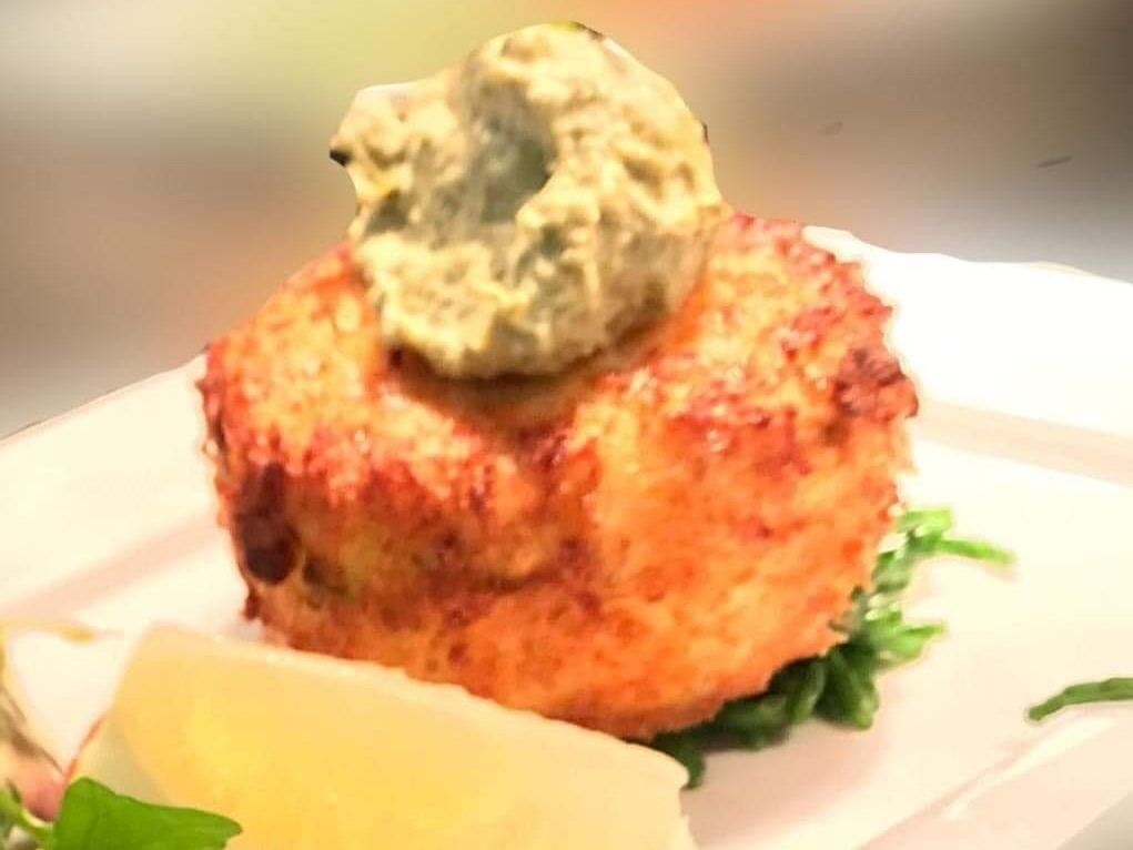 Um prato com um alimento redondo e dourado, provavelmente frito, coberto com uma porção de molho cremoso.