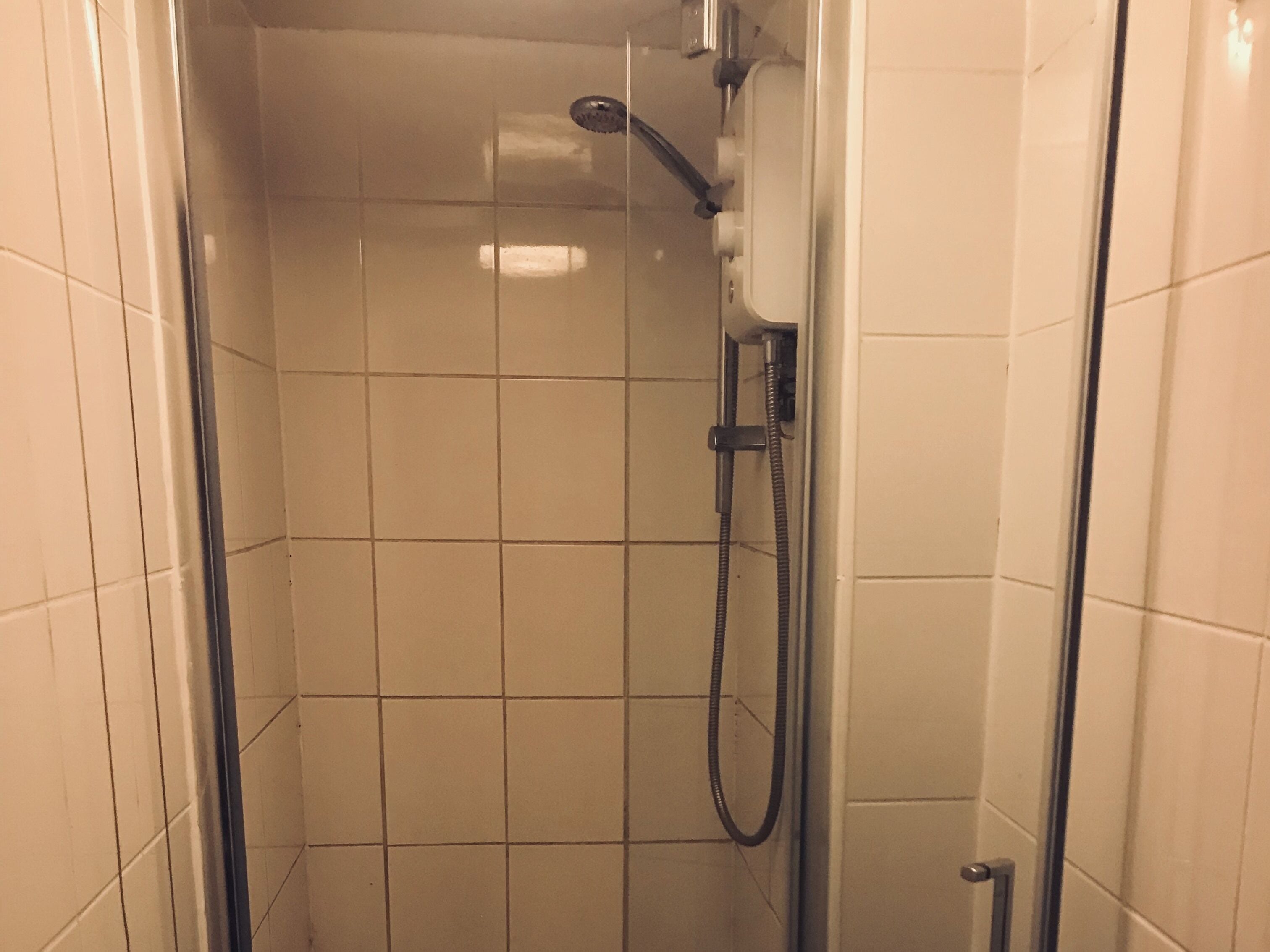 Um chuveiro pequeno revestido de azulejos, com um chuveiro manual e uma mangueira.