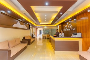 Uma área de recepção de hotel com design moderno, apresentando um balcão de atendimento, sofás e um painel decorativo com o contorno de montanhas.