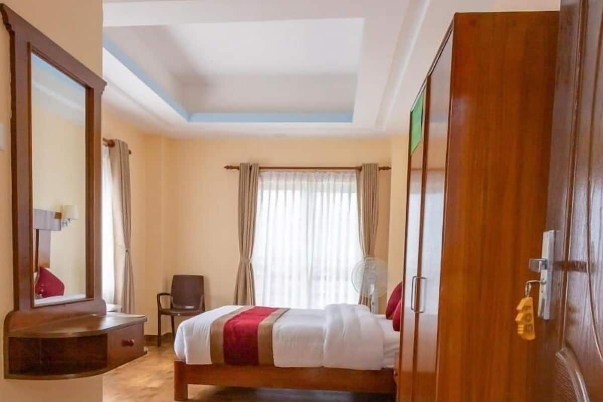 Quarto de hotel com cama, escrivaninha, cadeira, espelho e guarda-roupa.