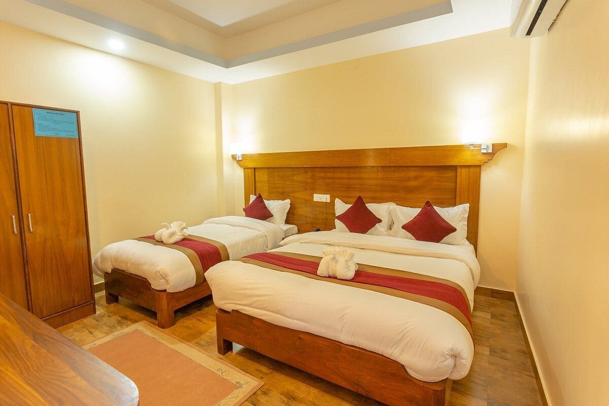 Quarto de hotel com duas camas, cabeceiras e guarda-roupa de madeira.