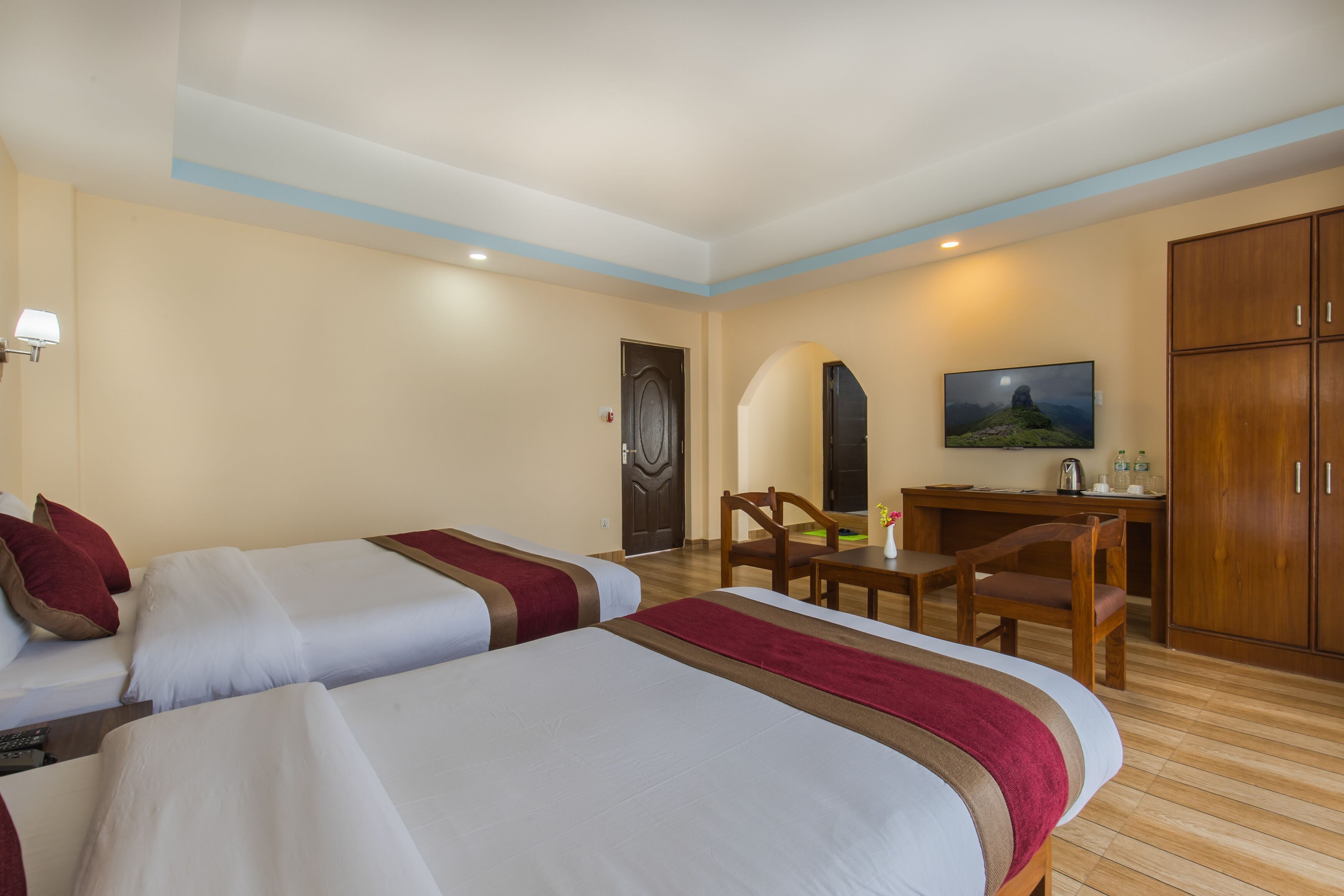 Quarto de hotel com duas camas, uma escrivaninha, uma cadeira, uma televisão e um guarda-roupa.