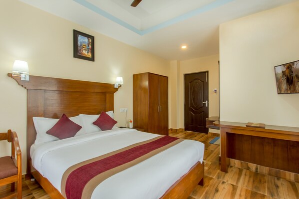 Quarto de hotel com cama de madeira, uma escrivaninha e uma porta.