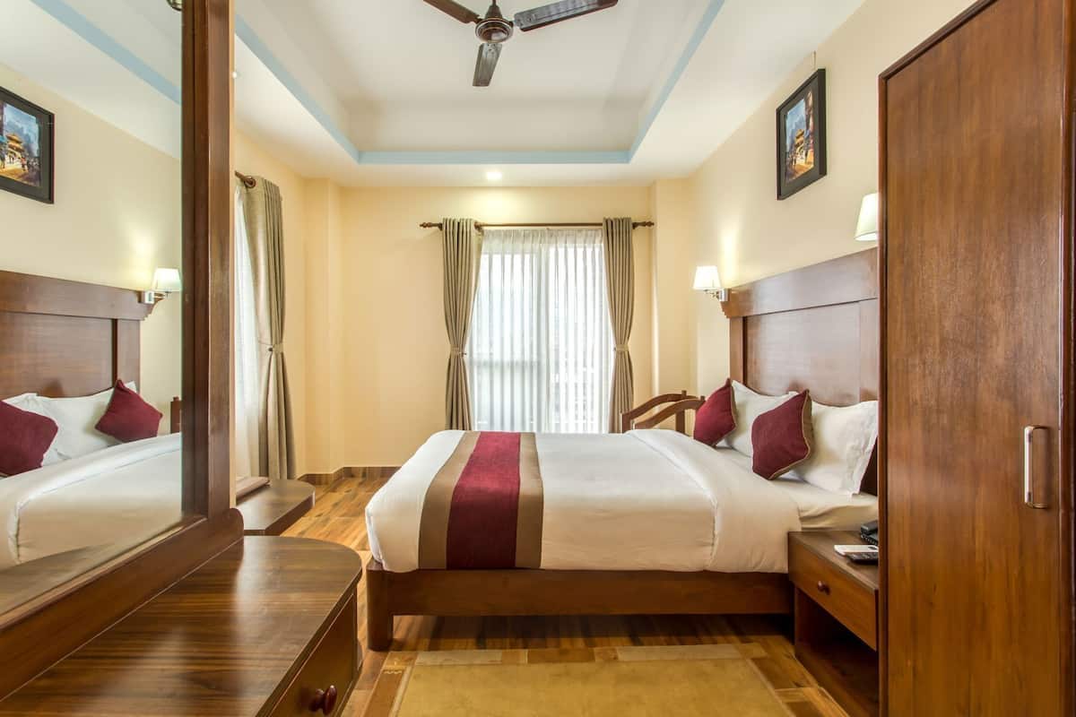 Quarto de hotel com duas camas, um ventilador de teto, um guarda-roupa de madeira e um espelho grande.