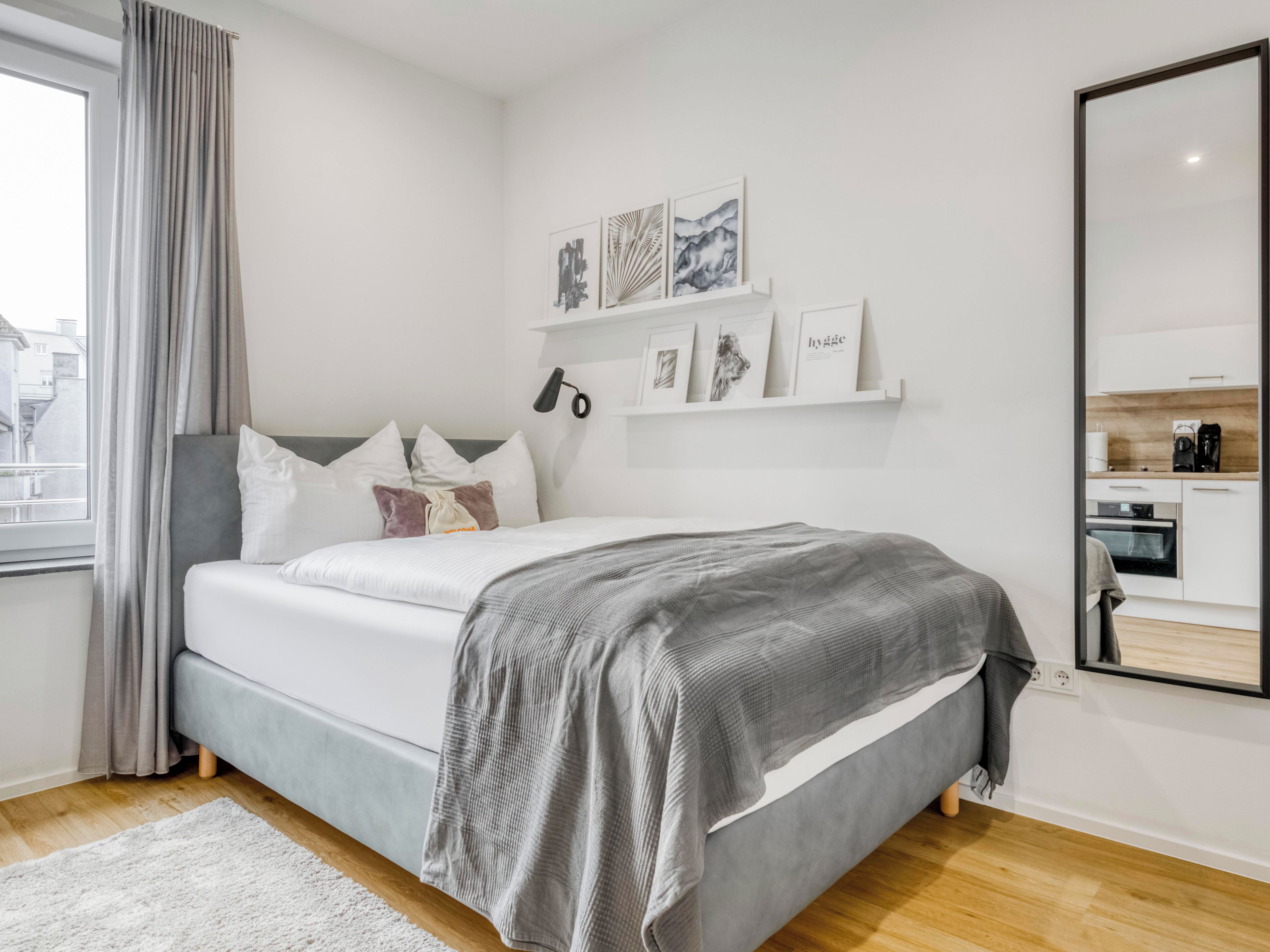 Quarto moderno com cama, mesa de cabeceira, espelho e prateleira com quadros.