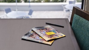 Revista sobre uma mesa com uma caneta, uma cadeira e vista para área externa.