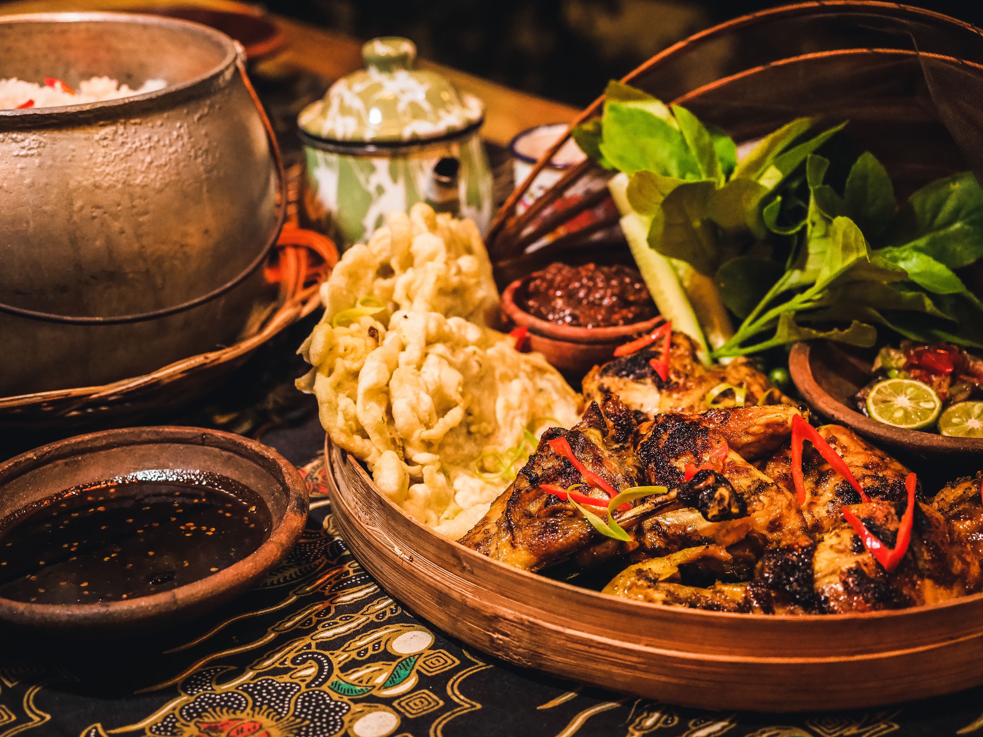 Diversos pratos, incluindo carne grelhada, frituras e um tacho de arroz, indicando uma variedade de opções gastronômicas.