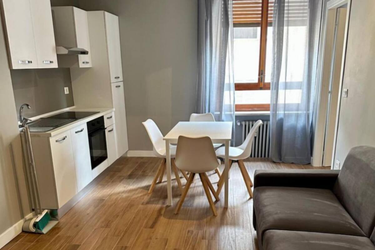 Um espaço compacto com cozinha compacta, mesa de jantar com cadeiras, sofá e janela com cortinas.