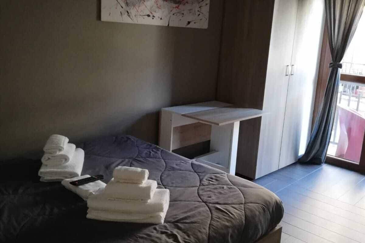 Quarto de hotel com cama, escrivaninha, cadeira, um quadro na parede e janela com cortinas.