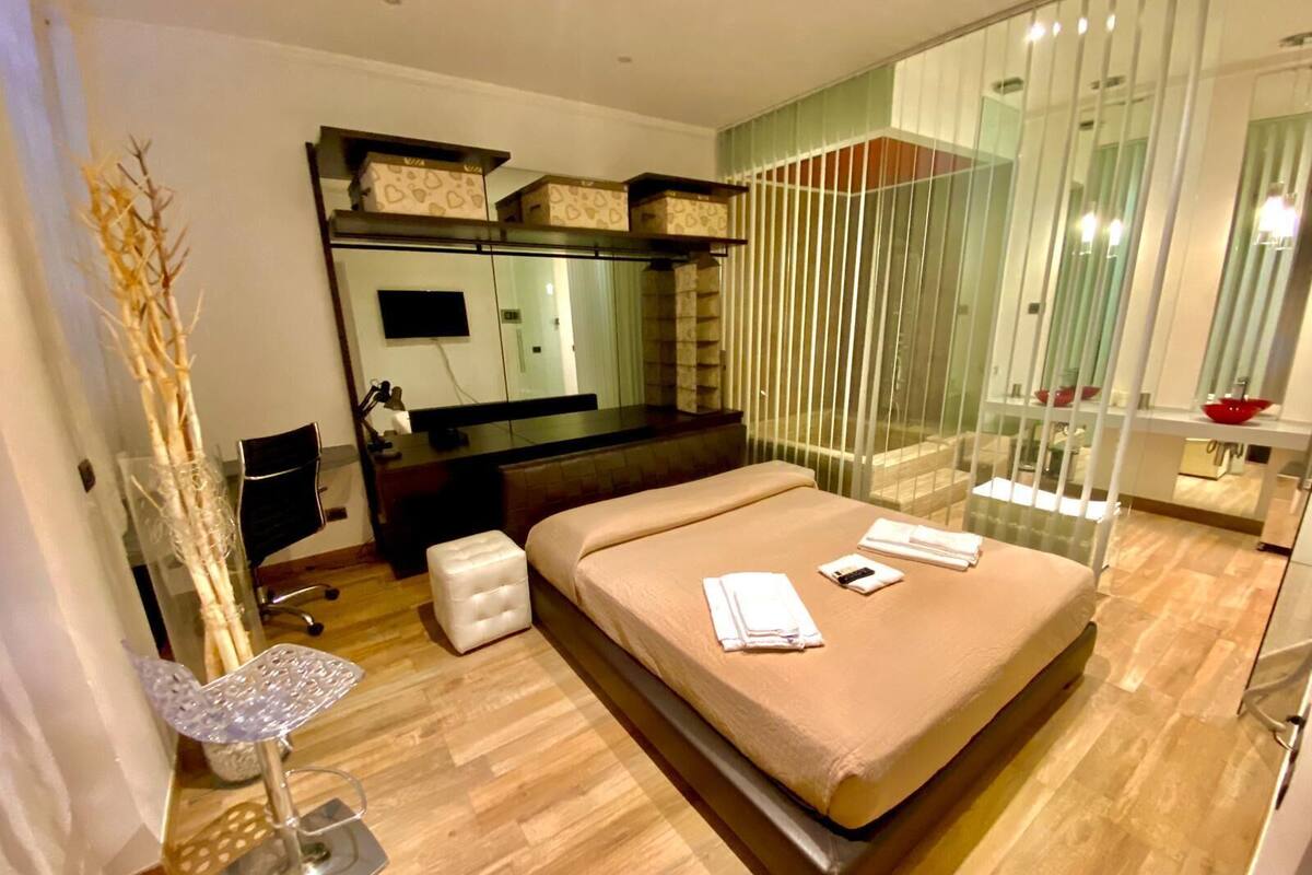 Quarto de hotel moderno com uma cama grande, uma escrivaninha, um espelho e vista pela janela.