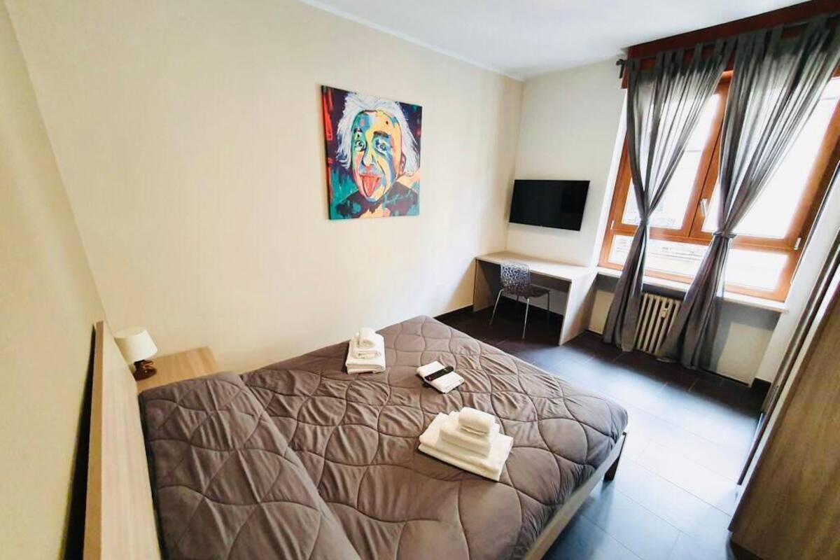 Quarto de hotel com cama, escrivaninha, televisão e um quadro na parede.