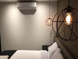 Quarto de hotel com cama, ar condicionado e luminária pendente de design exclusivo.