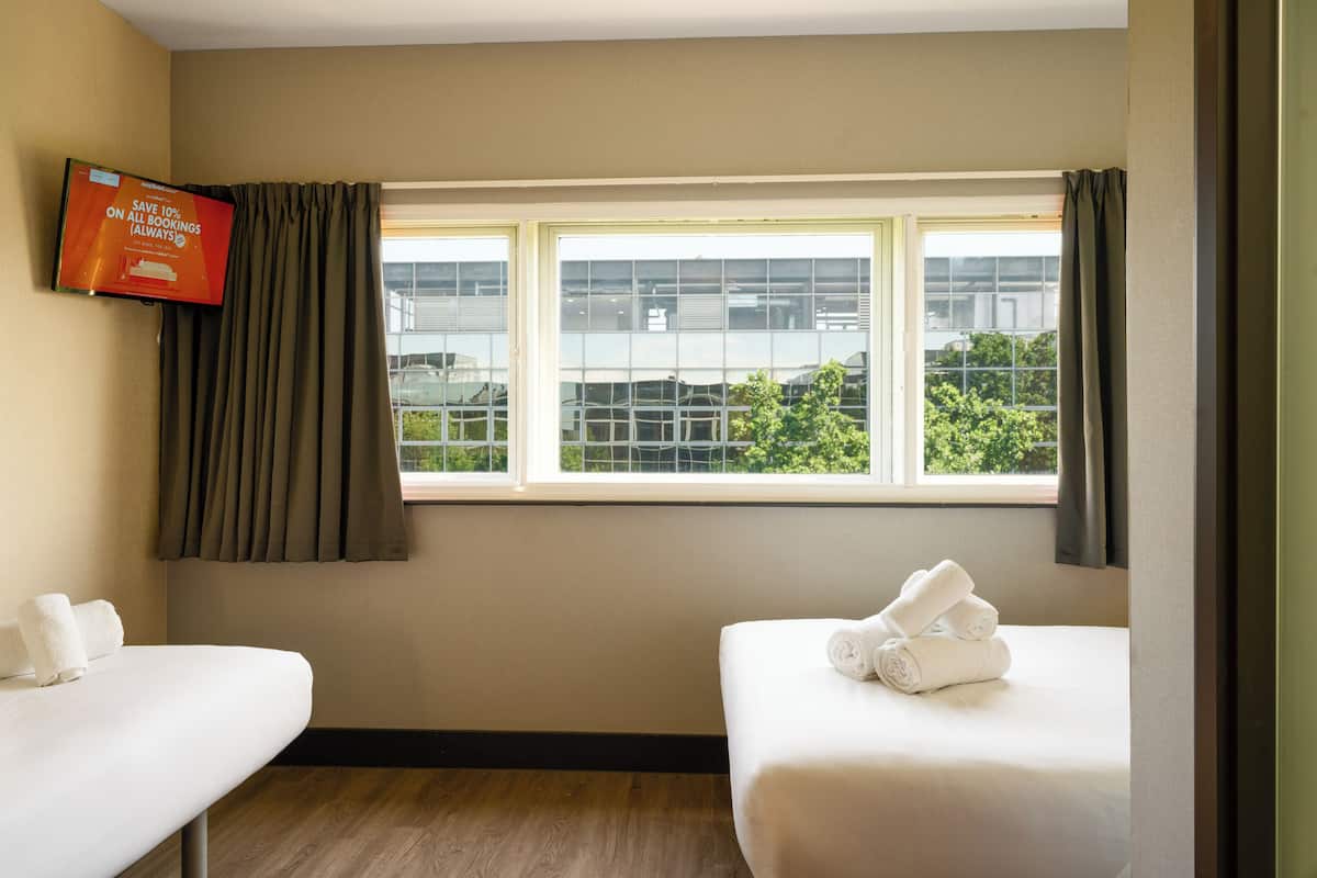 Quarto de hotel com duas camas, televisão na parede e janela com cortinas.