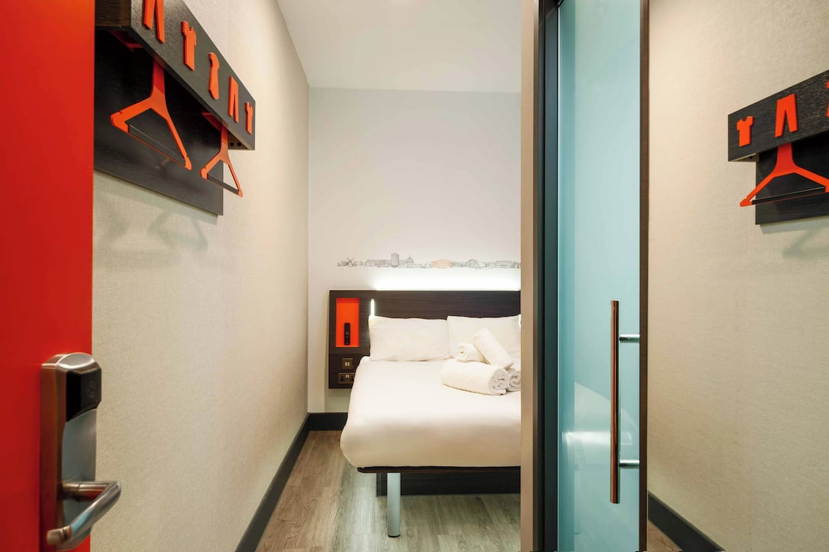 Quarto de hotel com cama, guarda-roupa e porta com puxador.