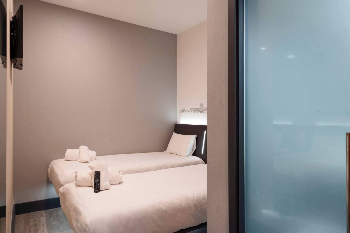 Quarto de hotel com duas camas, uma televisão de tela plana fixada na parede e janela com vista para um edifício.