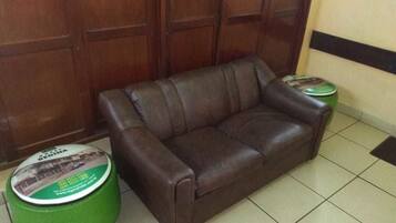 Um sofá de couro marrom com um banquinho verde e uma lixeira em um quarto com painéis de madeira e piso de azulejos.