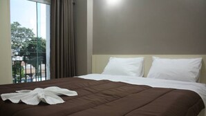 Quarto de hotel com uma cama grande, vista para o exterior através de uma janela e uma varanda.