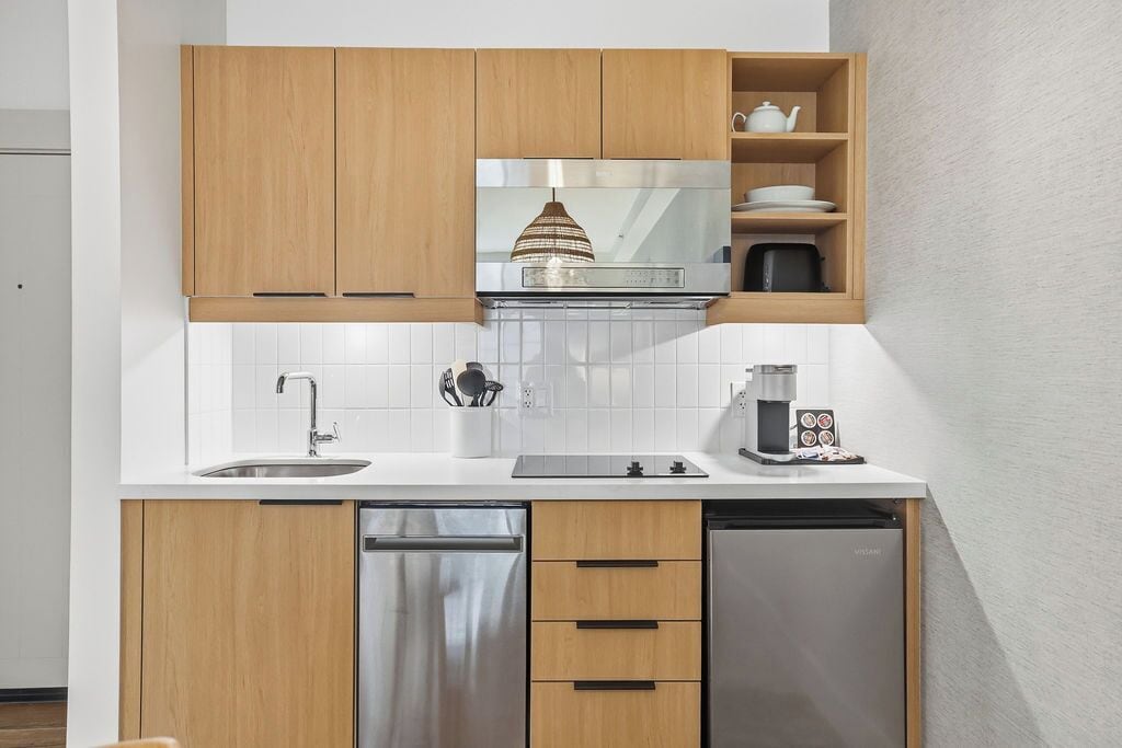 Cozinha compacta com armários de madeira, lava-louças de aço inoxidável, pia e cafeteira.