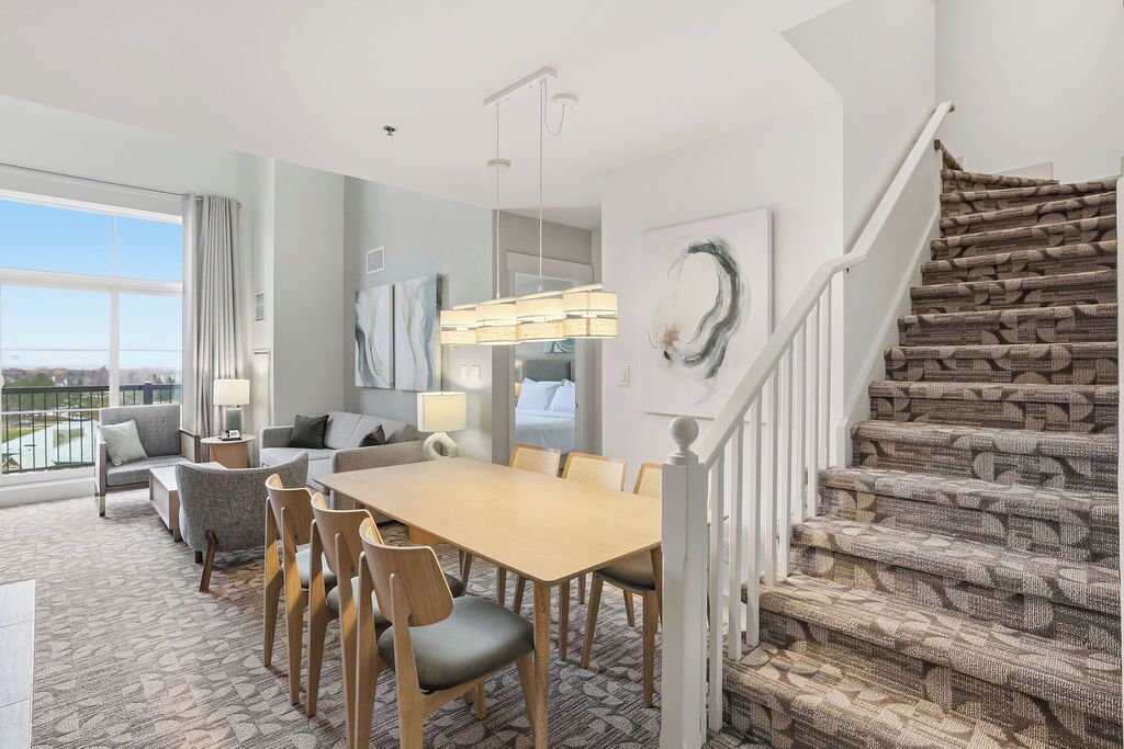 Quarto de hotel moderno com área de refeições, escada e vista para o exterior.