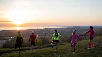 Um grupo de pessoas correndo numa colina gramada, com o pôr do sol ao fundo.