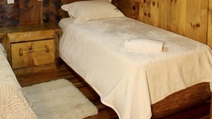 Quarto de cabana de madeira com duas camas, uma mesa de cabeceira e um tapete branco.