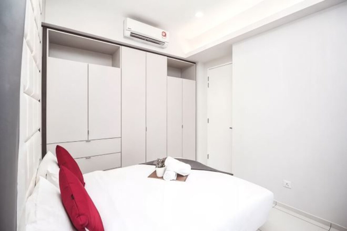 Quarto de hotel com cama, travesseiro vermelho, um gato, toalha branca e um guarda-roupa.