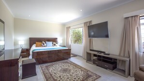 Quarto moderno com cama grande, televisão de tela plana, móvel para TV e uma janela ampla com cortinas.