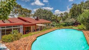 Uma piscina com uma casa de telhado vermelho e um espaço coberto de varanda.