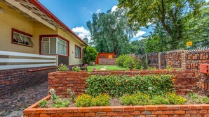 Um imóvel residencial com jardim de tijolos, cerca de madeira e casa com telhado vermelho.