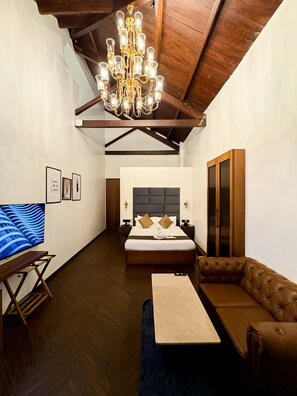 Quarto de hotel com uma cama grande, teto de madeira, lustre, televisão e sofá.