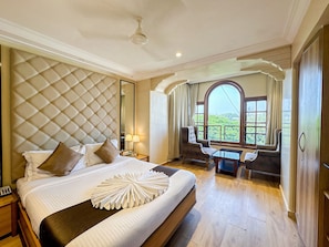 Quarto de hotel com uma cama grande, vista para o verde, varanda e ventoinha no teto.