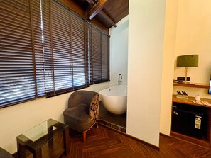 Um banheiro com banheira, uma cadeira, uma mesa de vidro e um armário com artigos de higiene pessoal.