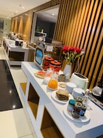 Buffet de café da manhã com diversos alimentos, uma máquina de café e uma torradeira.