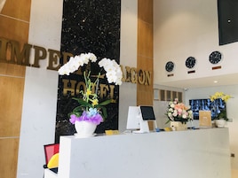 Balcão de recepção de hotel com uma grande placa indicando "IMPERIAL HOTEL", um monitor de computador, um leitor de cartão Samsung Pay e um arranjo floral.