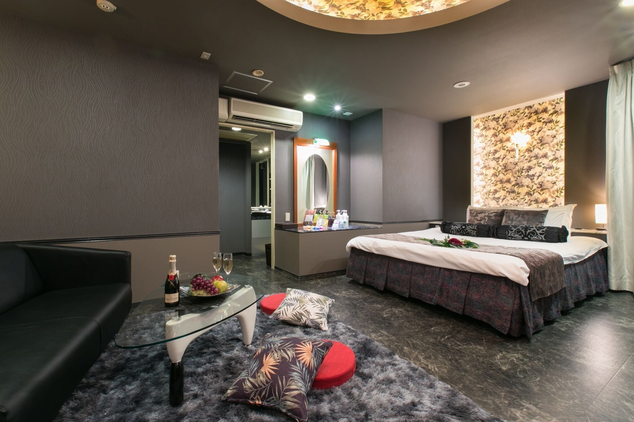 Quarto de hotel moderno com cama, sofá, mesa de centro de vidro e um móvel com comodidades.