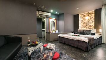 Quarto de hotel moderno com cama, sofá, mesa de centro de vidro e um móvel com comodidades.