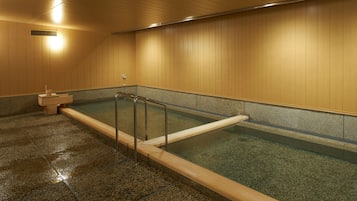Uma sauna com banco de madeira, corrimão de metal e chão revestido de azulejos.
