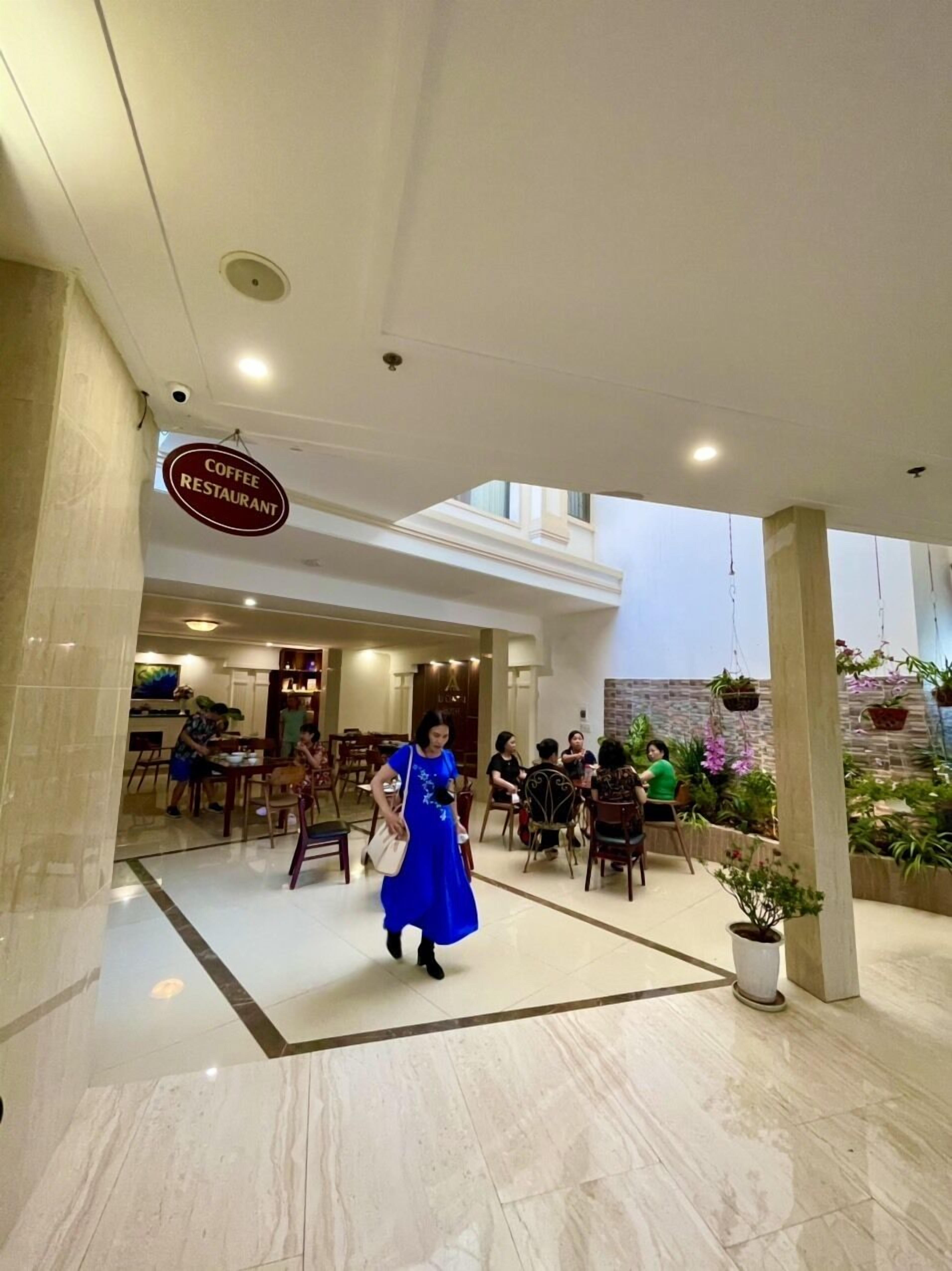 Um espaço amplo e interno com um restaurante de café, piso de mármore e área de estar com mesas e cadeiras.