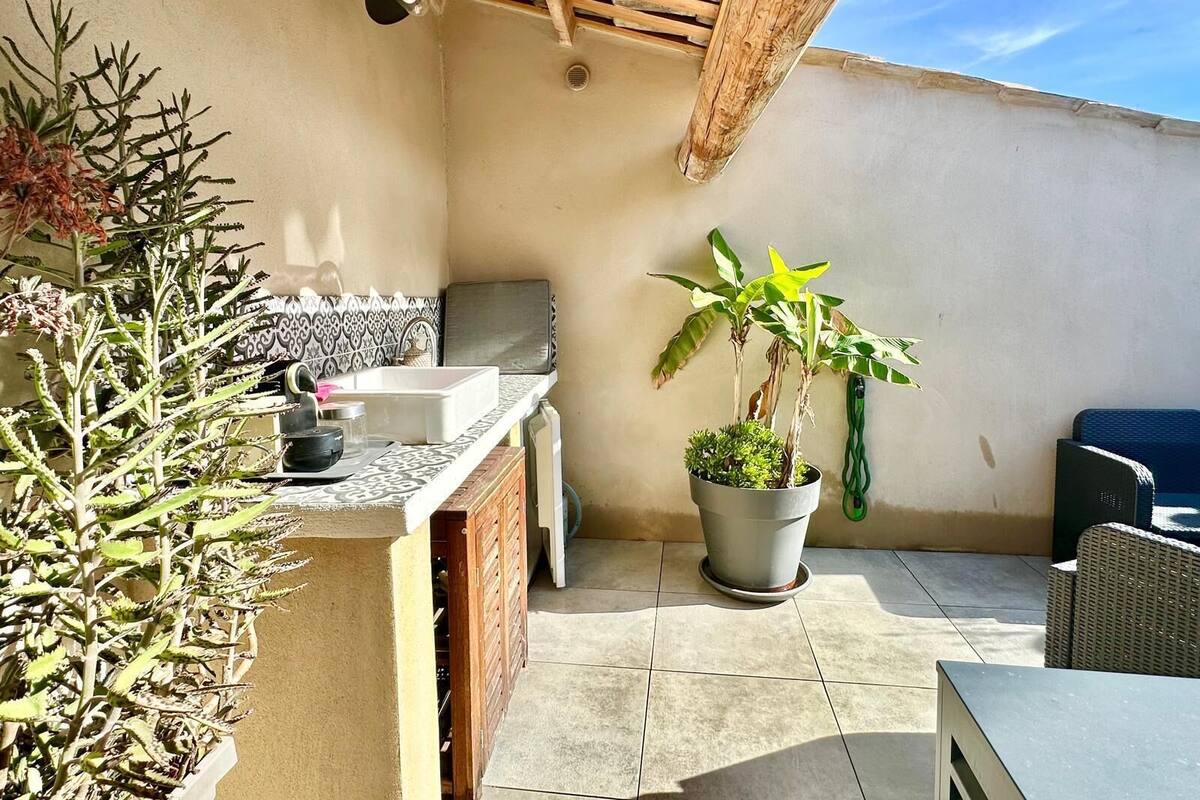 Uma pequena área de cozinha ao ar livre com pia, prateleira de madeira e um vaso com planta.