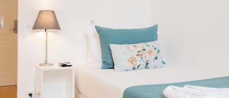 Quarto bem organizado com cama, mesa de cabeceira com luminária, prateleira pequena e quadro na parede.
