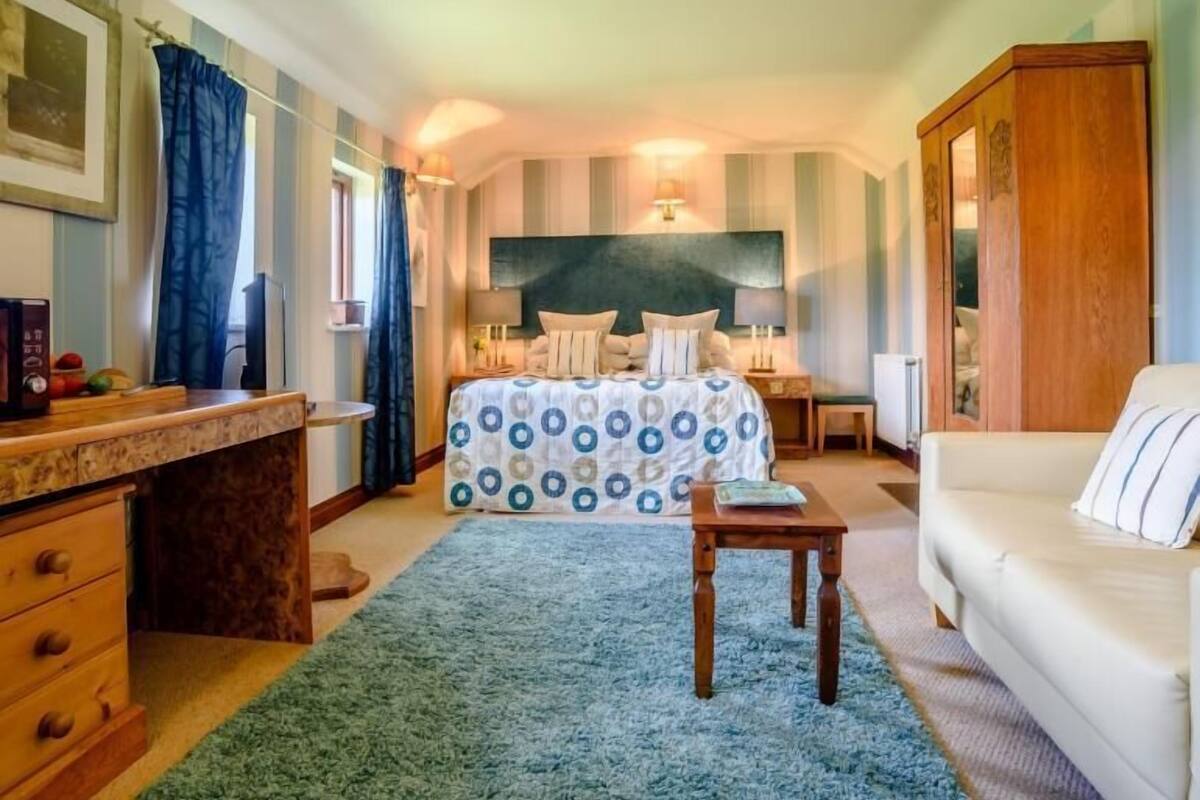 Quarto de hotel com cama, escrivaninha, cadeira, sofá e espelho.