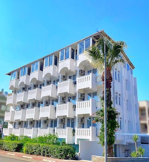 Um hotel com vários andares, varandas, aparelhos de ar condicionado e uma palmeira na frente.