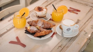 Uma mesa com doces, uma xícara de café e dois copos de suco de laranja.
