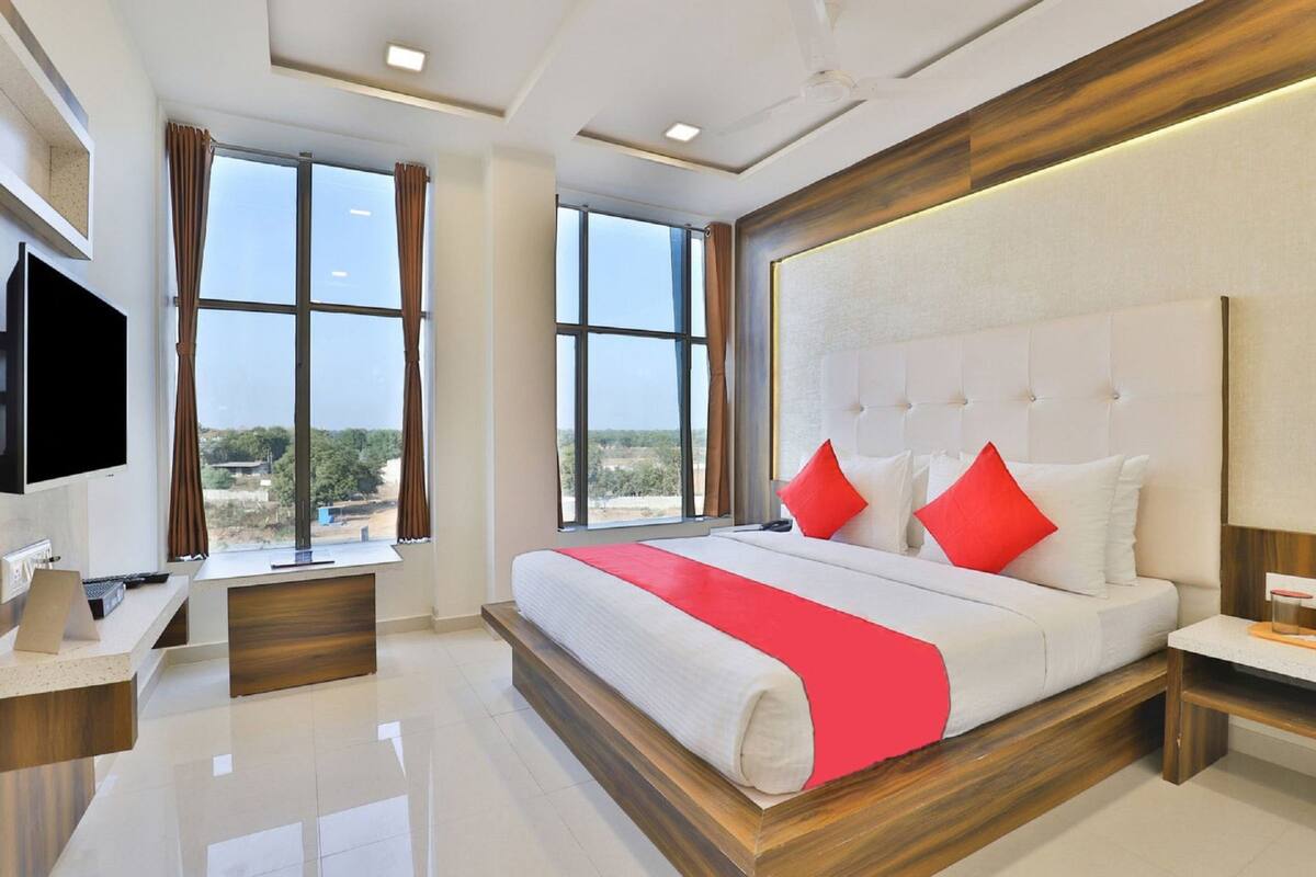 Quarto de hotel moderno com uma cama grande, televisão de tela plana, escrivaninha e janelas amplas com vista para o exterior.