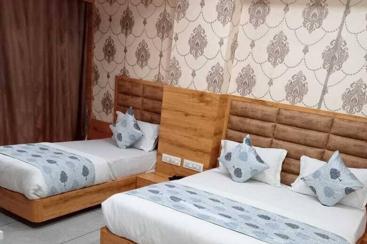 Duas camas de madeira com cabeceiras iguais, roupa de cama branca e almofadas com padrão de folhas cinzas.