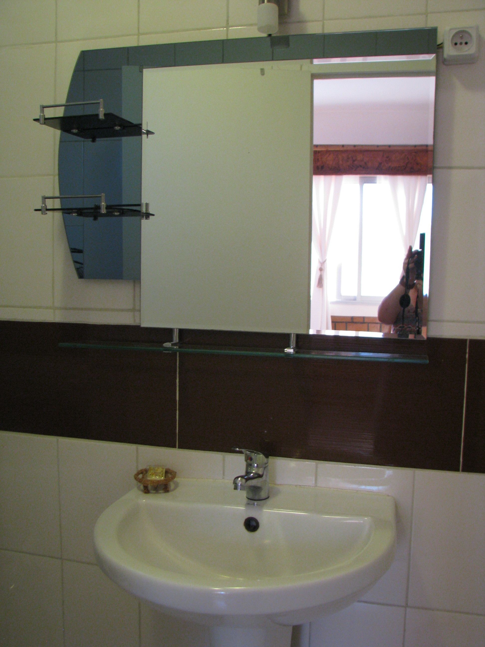 Casa de banho com uma pia branca, espelho e janela com cortinas.