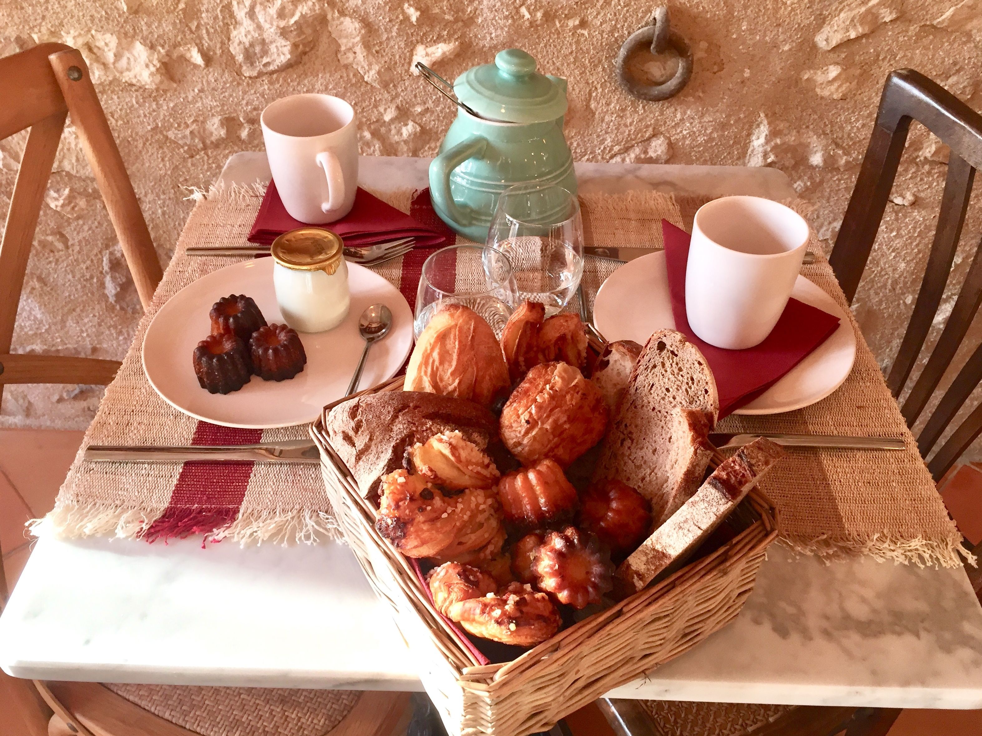 Uma mesa posta com uma cesta de doces, duas xícaras, um bule e um prato com sobremesa.