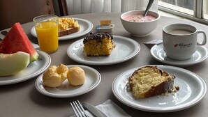 Uma mesa de café da manhã com pratos de comida, um cereal em uma tigela, um copo de suco de laranja, uma xícara de café e um conjunto de garfo e faca.